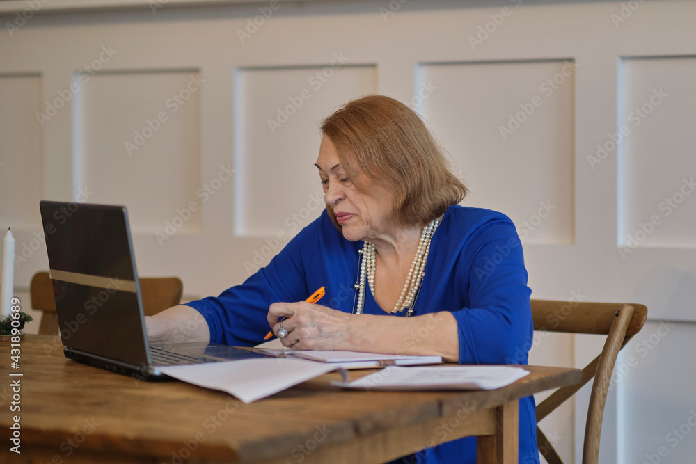 Senior woman using laptop for websurfing in her kitchen. The concept of ...