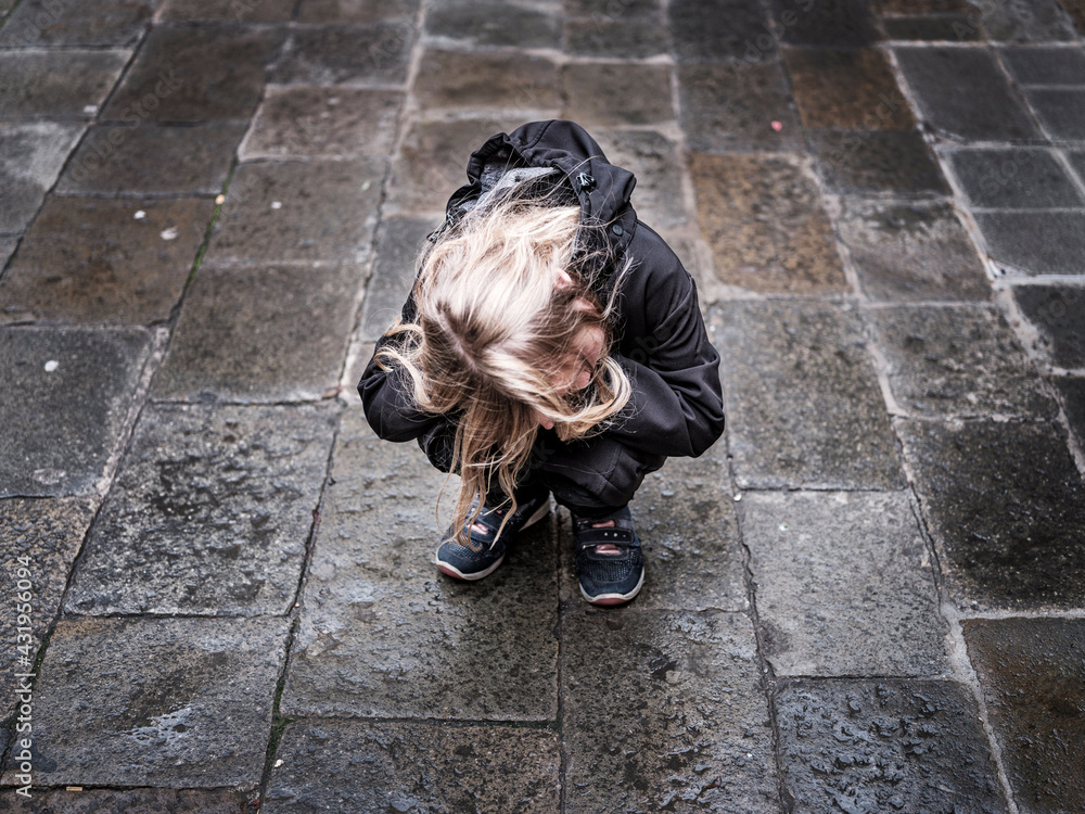 Sad lost girl crying while crouching on footpath during rainy season ...