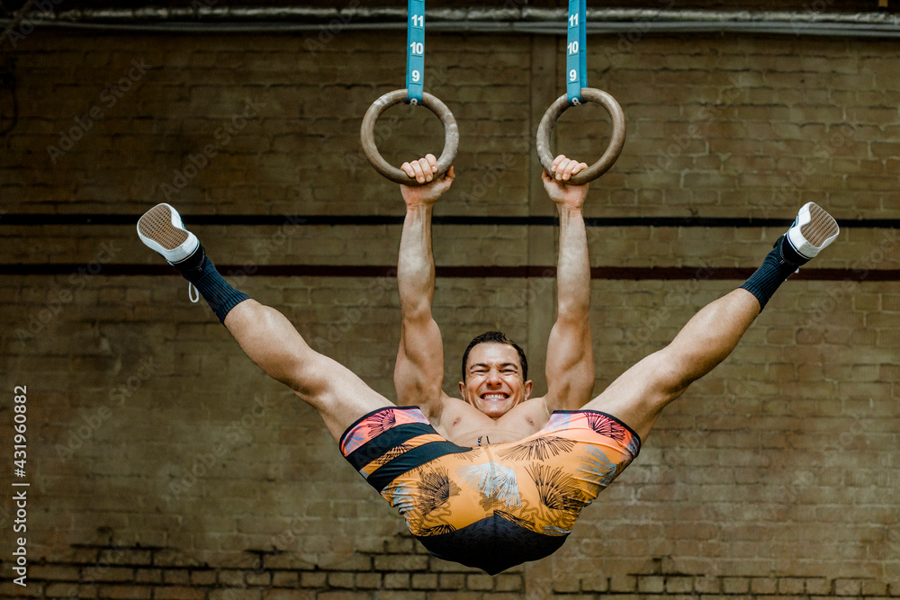 Excited male athlete with leg split hanging through gymnastic rings at ...