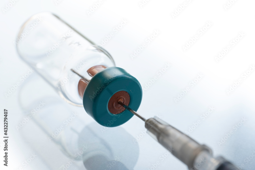 Syringe needle protrudes through the red rubber cap of a vaccine bottle ...