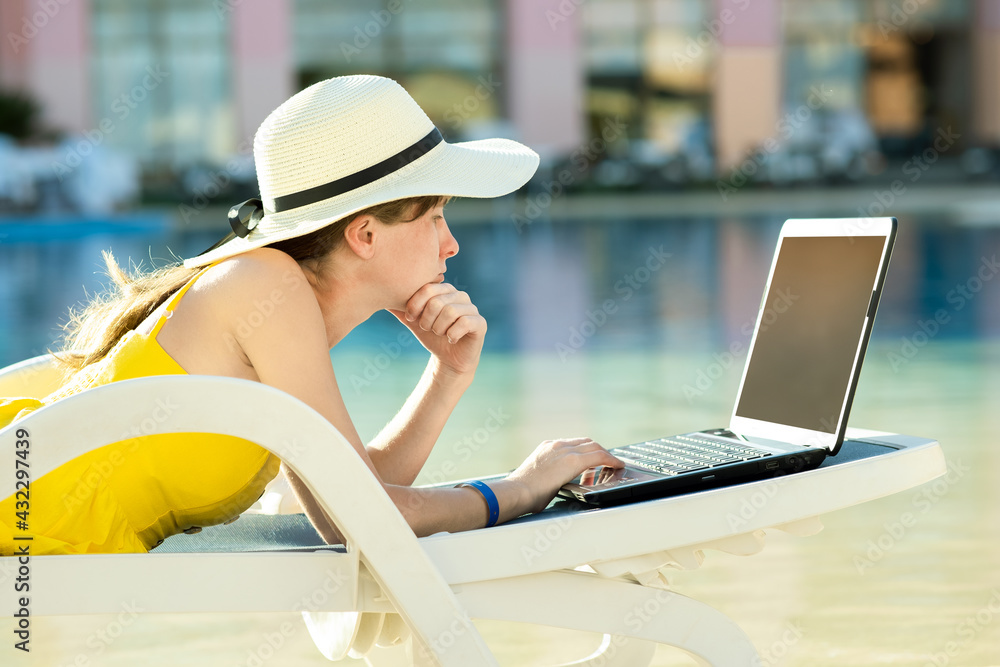 Young woman on beach chair at swimming pool working on computer laptop ...