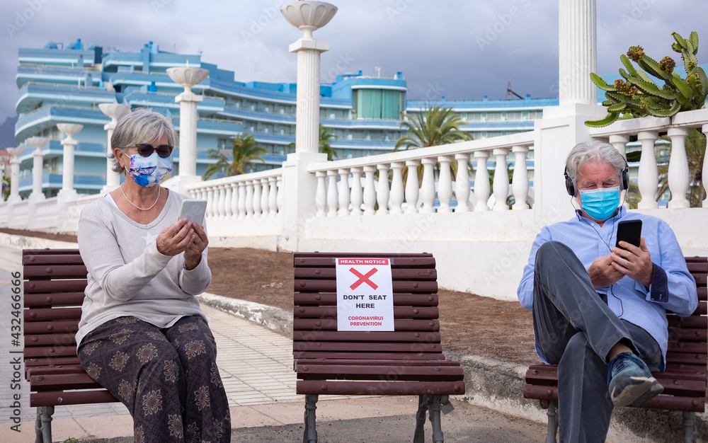 Social distancing concept. Two senior people sitting outdoor on allowed ...