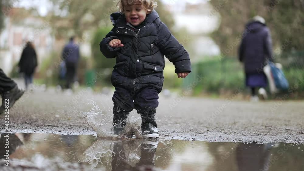 Cute toddler jumping into puddle of water. Adorable child boy playing ...