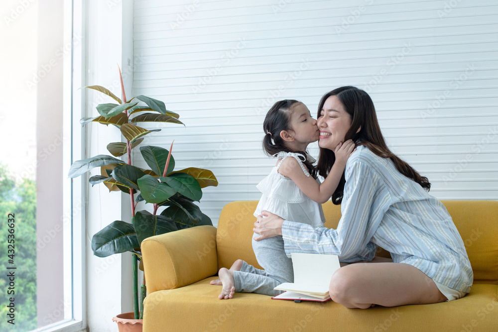 Sweet little girl kissing her mom while sitting on couch at home, family spend time together ...