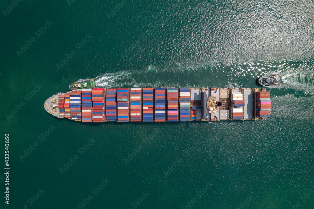 Aerial in front of cargo ship carrying container and running with tug ...