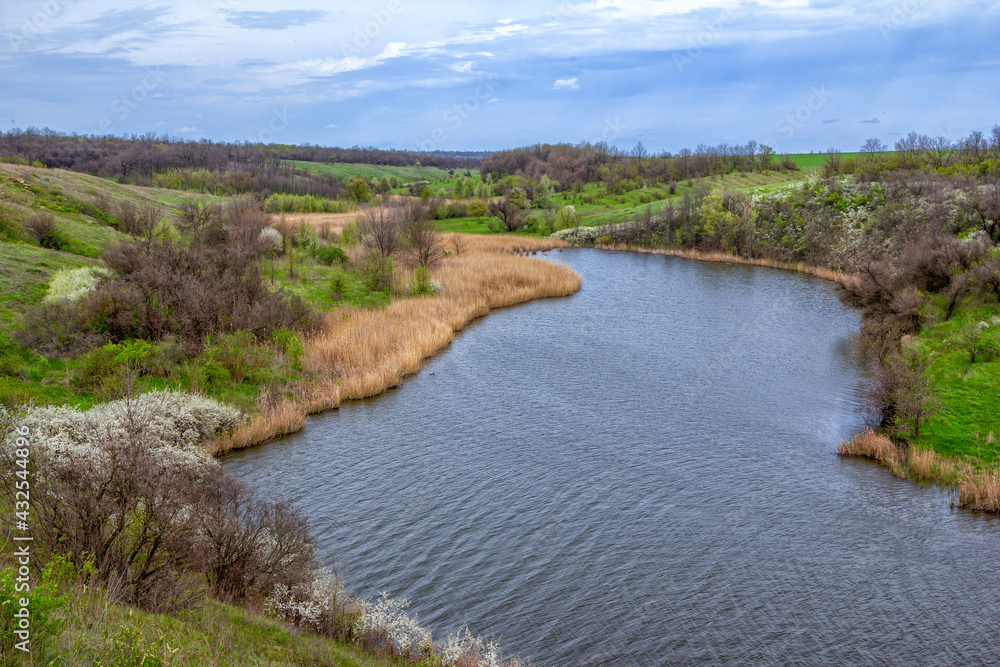 Beautiful spring landscape with river, coast with dry reeds and hills ...
