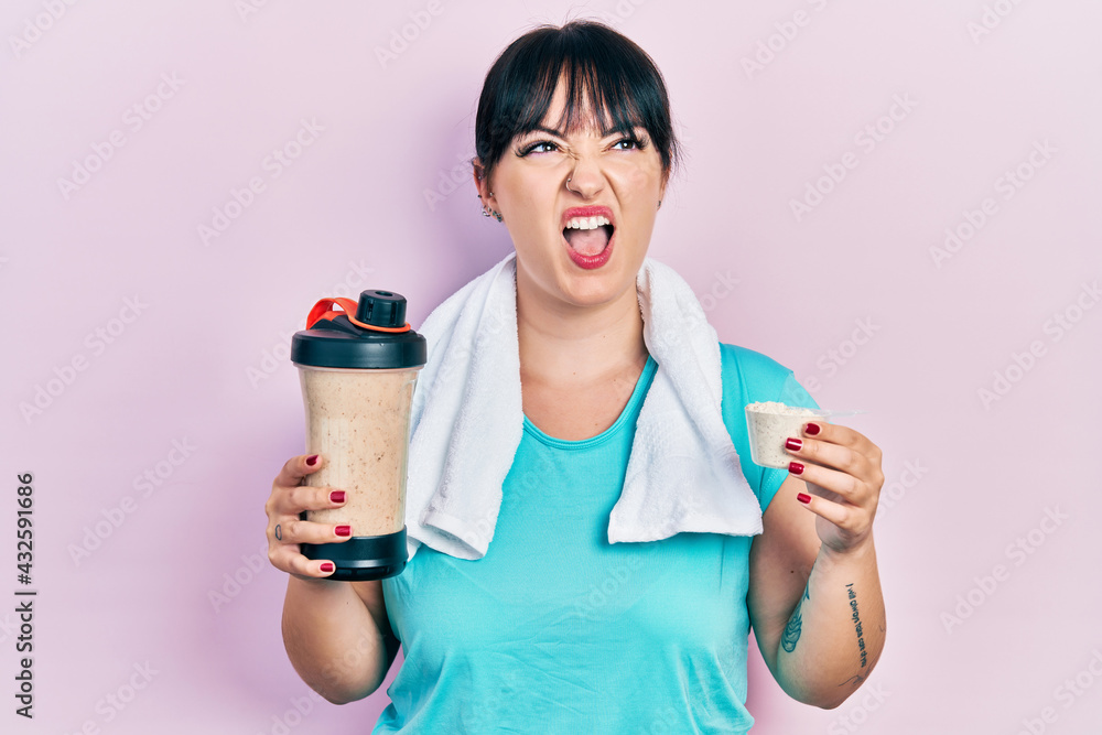 Young hispanic woman wearing sportswear holding water bottle angry and ...