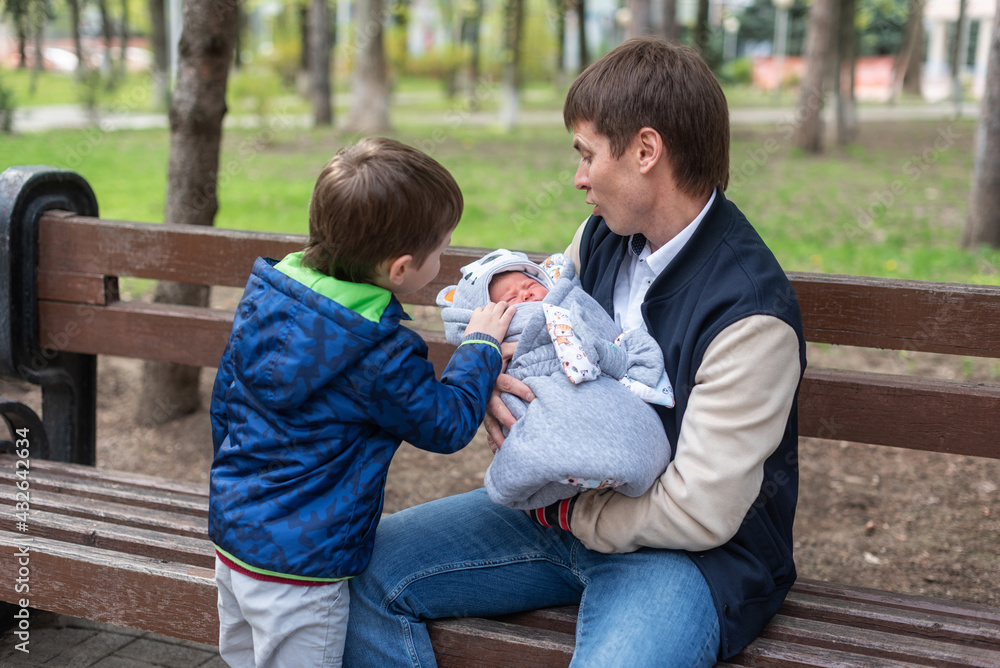 A Young Father With A Newborn In His Arms Shows His Eldest Son His New Brother Discharge From