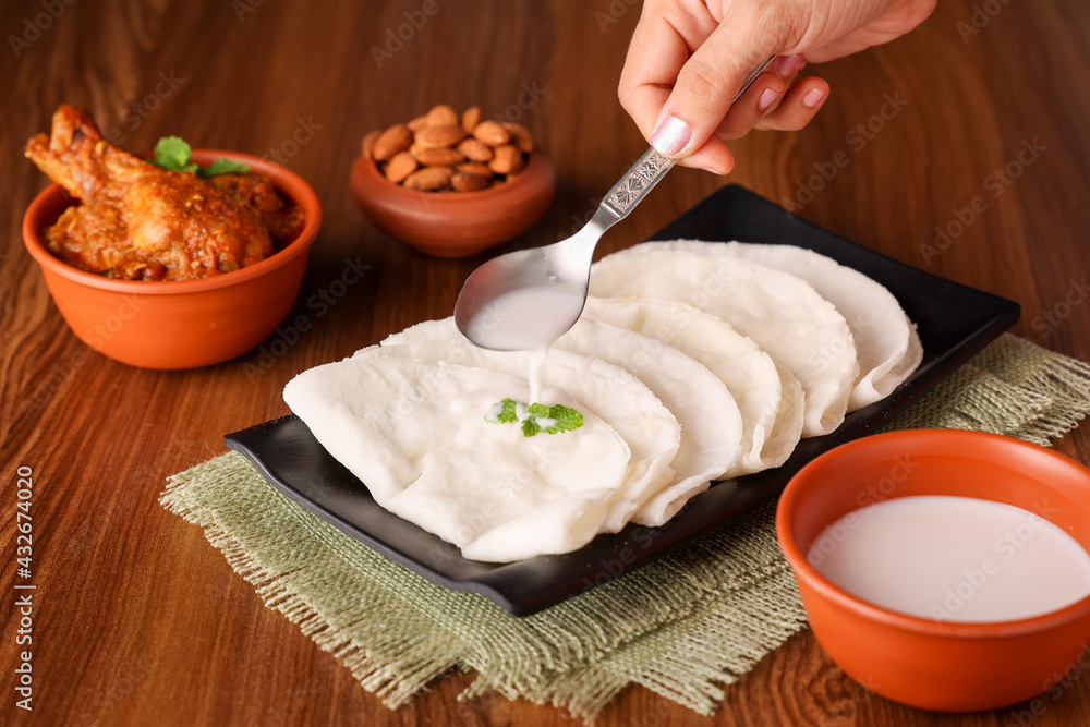 Hand pouring coconut milk on Rice pathiri Pathiri Indian flatbread ...