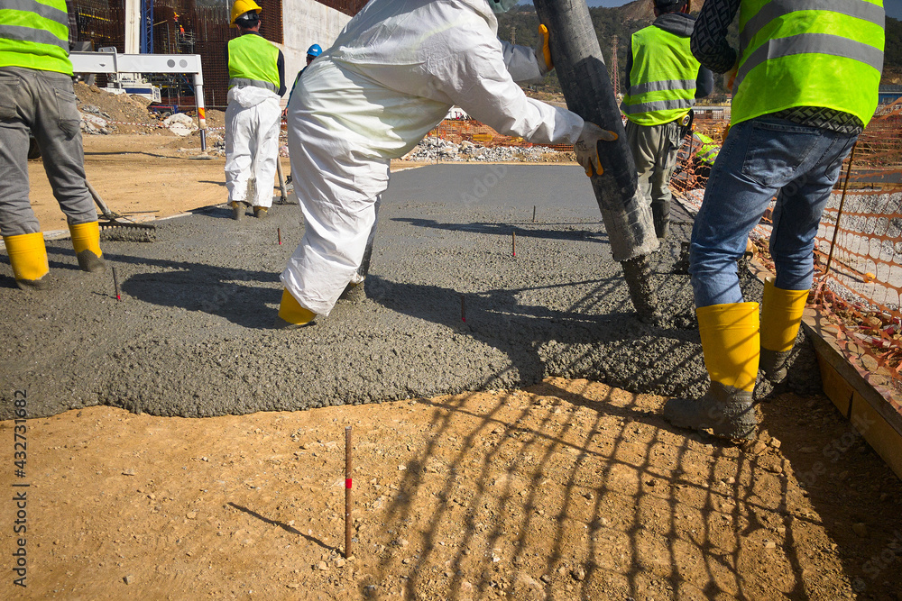 Construction workers dressed in uniform pour a concrete to formwork ...