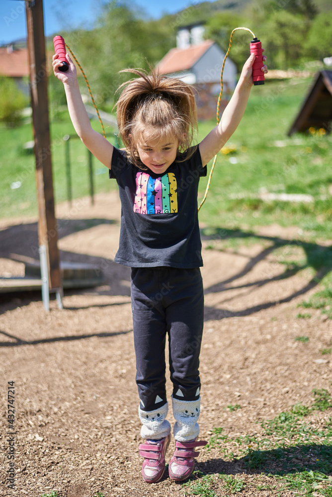 cute little girl playing, jumping on a rope outdoor in playground ...