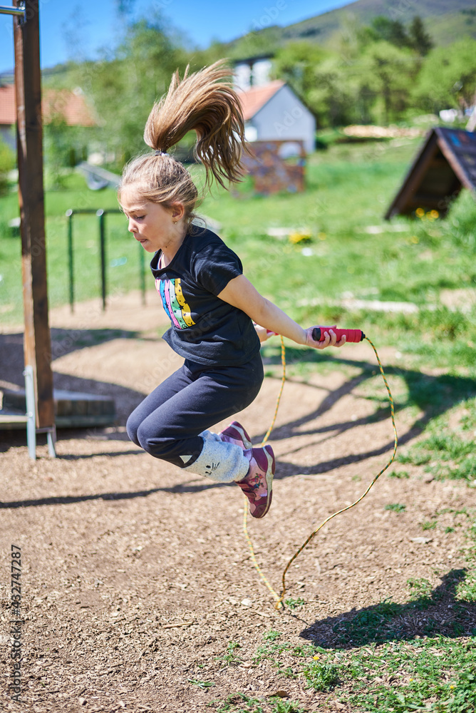 cute little girl playing, training, jumping on a rope outdoor in ...