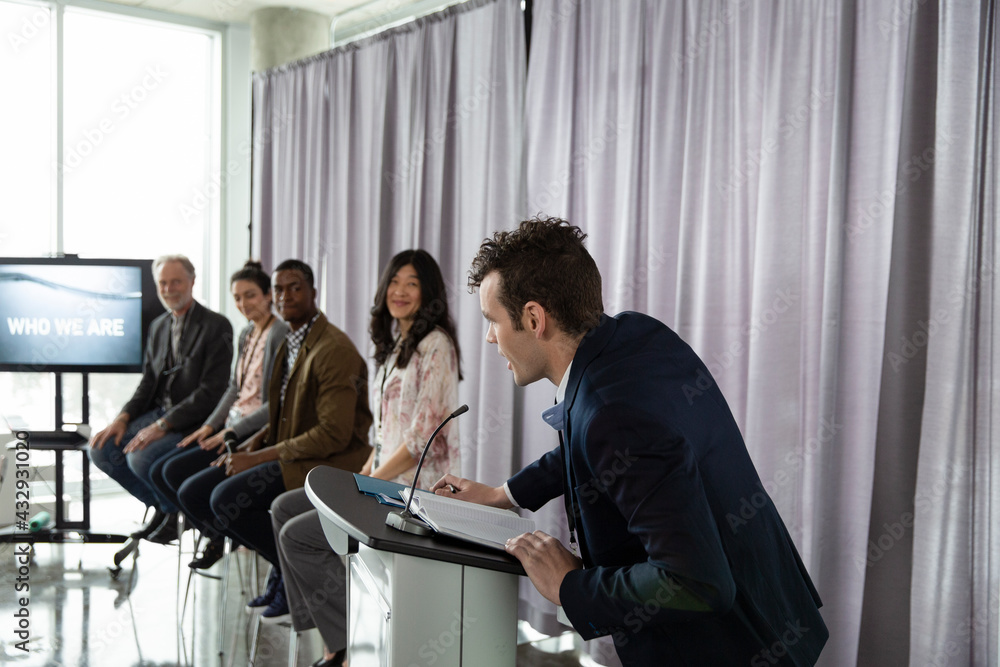 Man at podium introducing panel of motivation speakers at conference ...