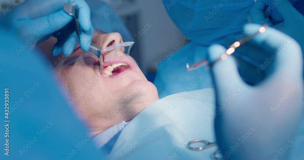 Close-up an adult male patient is under anesthesia while the dentist is ...