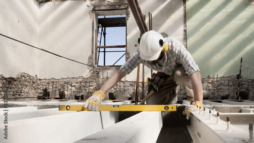 man at work, construction worker wears helmet and uses the spirit level ...