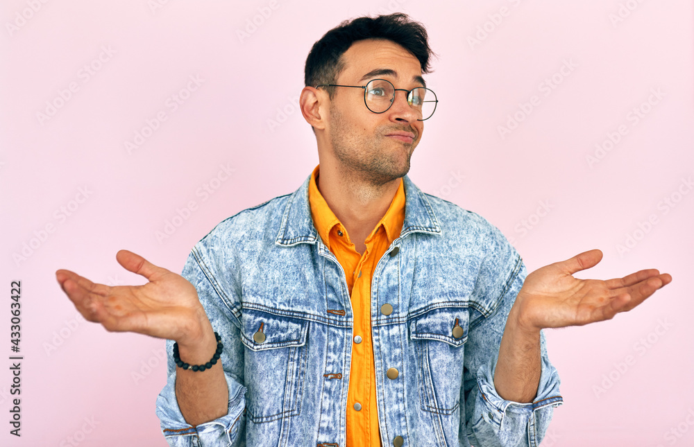 Confused young man spreads hands sideways, smirks face, isolated over a ...