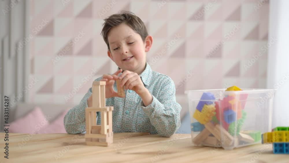 Happy cute little caucasian boy playing game building constructor tower ...
