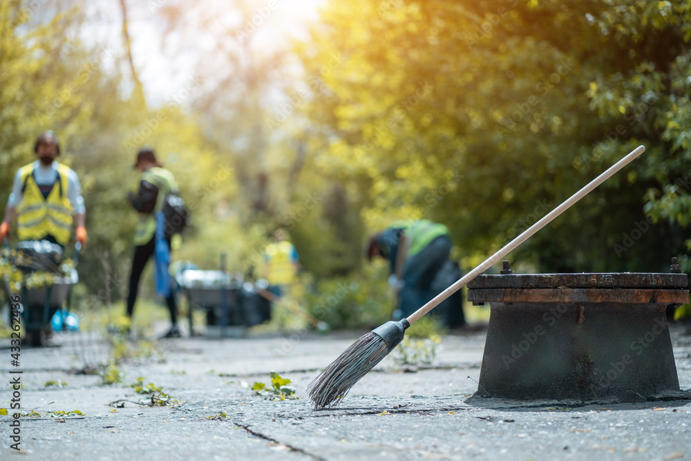 broom lying on street, volunteers cleaning up park from dust, waste and ...