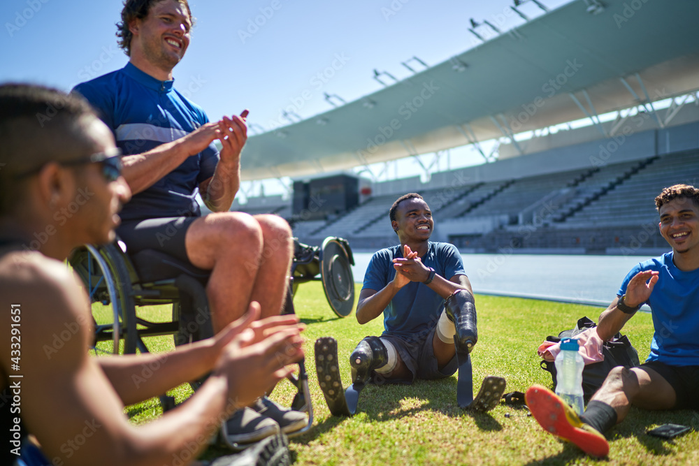 Paraplegic and amputee male athletes clapping on sunny stadium grass ...