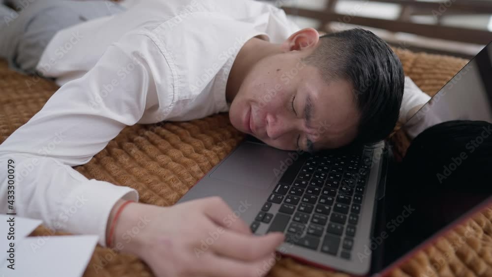 Tired young Chinese man yawning lying on laptop keyboard napping in ...