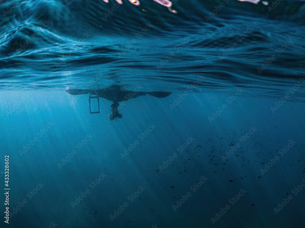 Underwater view of a boat bottom part and fishes swimming in clear blue ...