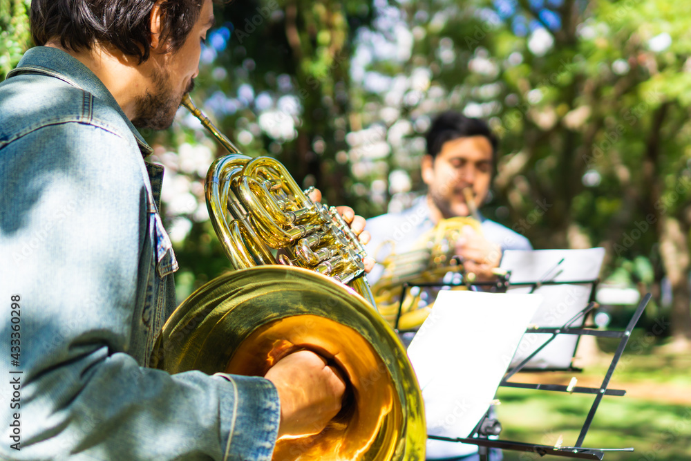 latin man playing a french horn in the park while rehearsing with sheet ...
