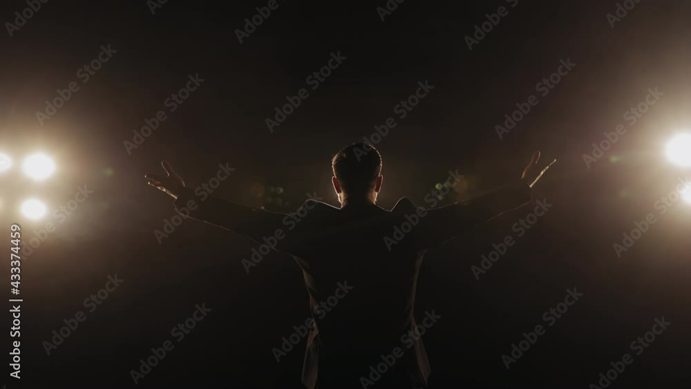 The speaker is standing on stage and holding up his hands. The ...