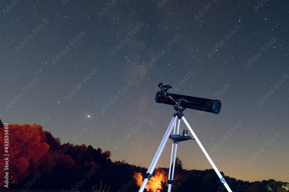 Black telescope reflector on a tripod in starry night sky scene ...