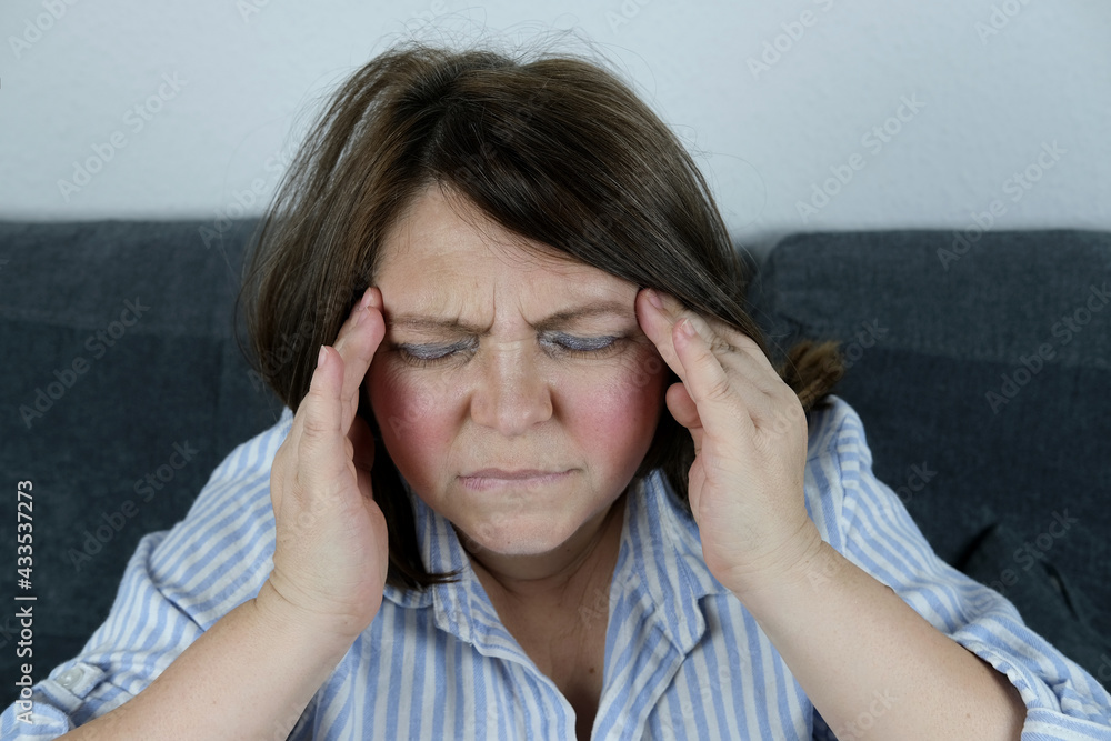 adult woman sits on a sofa, covered with a blanket, clasped her head in ...