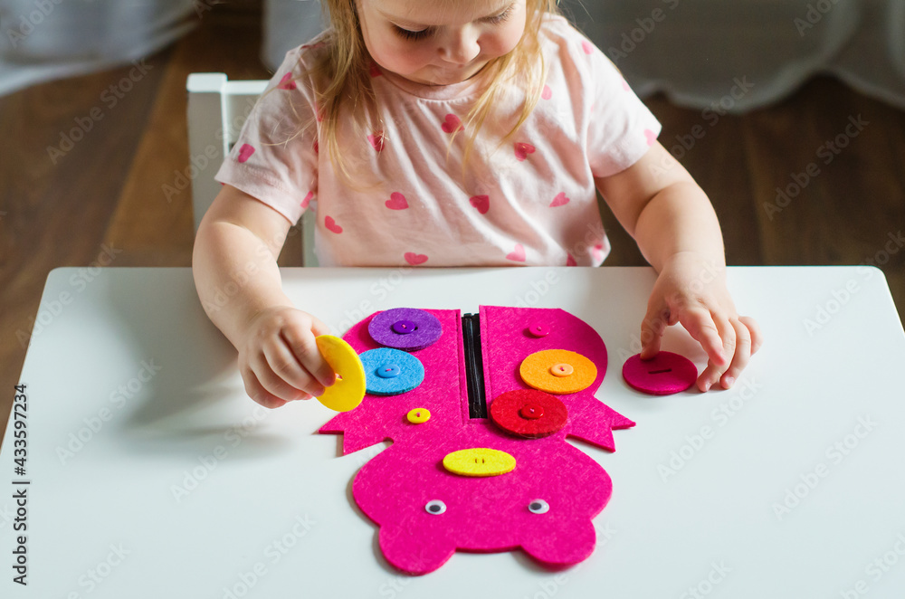 Little toddler girl buttoning a Montessori toy. Practical life skills ...