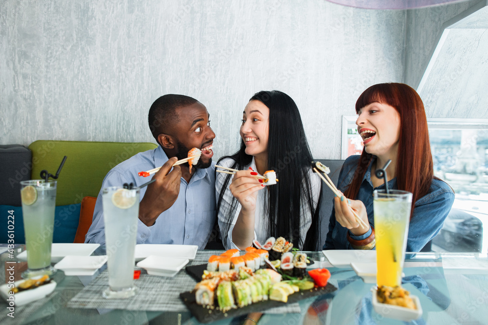 Happy three multiracial friends enjoying sushi at a Japanese restaurant ...