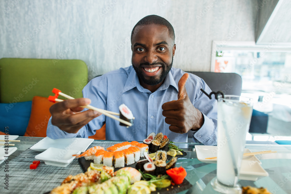 Young smiling African American handsome man eating sushi using ...