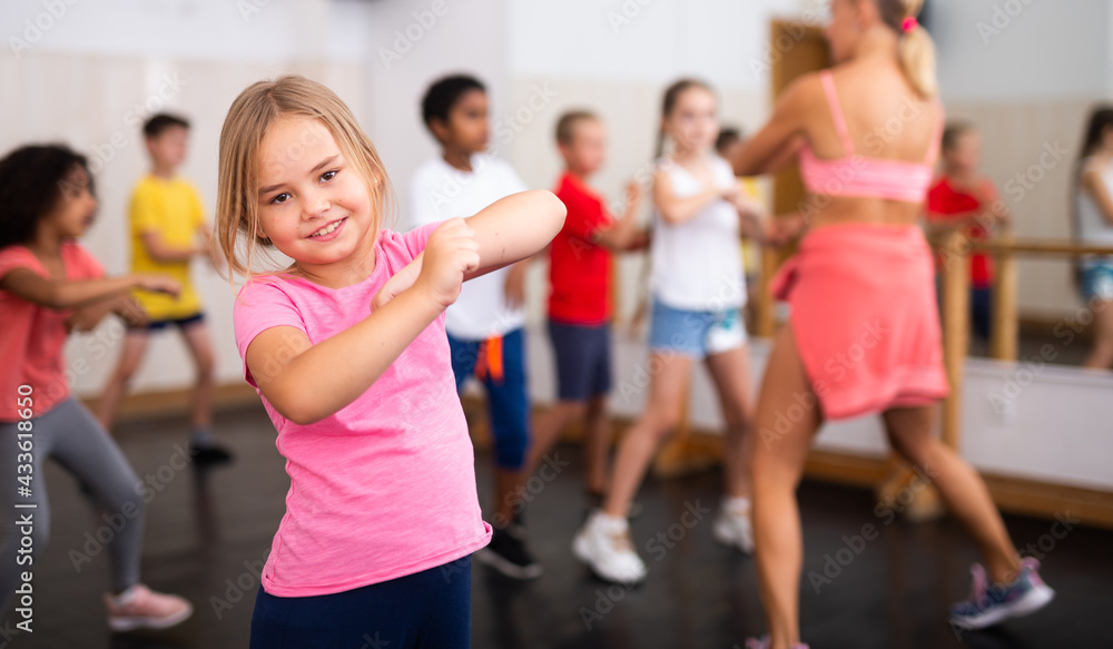 Smiling little girl training movements of vigorous dance with group of ...