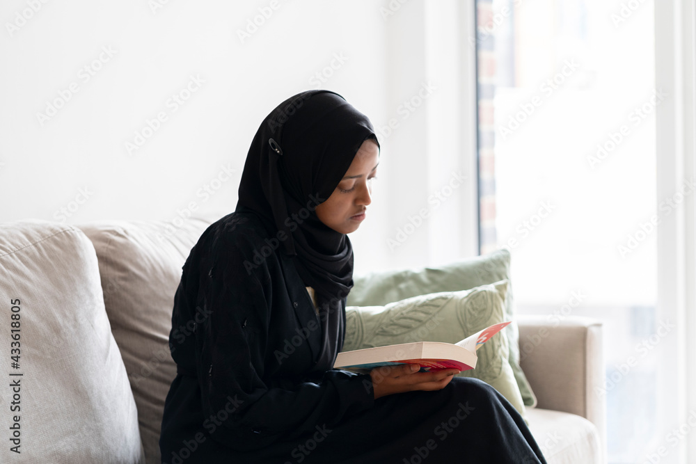 Black Muslim teenage girl reading a book in the living room Stock Photo ...