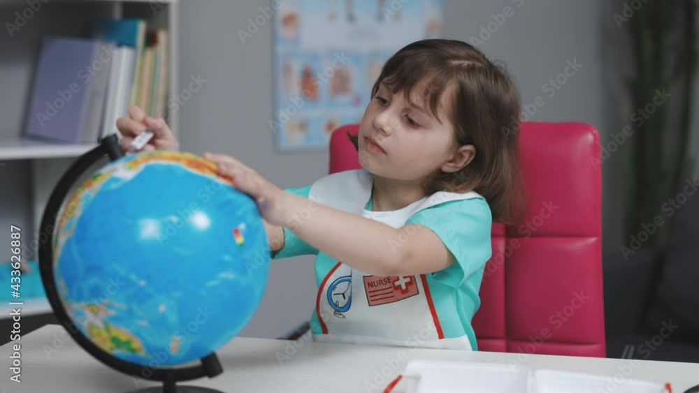 Little kid girl dressed in a doctor's suit measures the temperature of ...