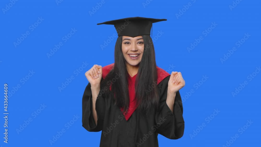 Portrait of female student in graduation costume looking at camera with ...