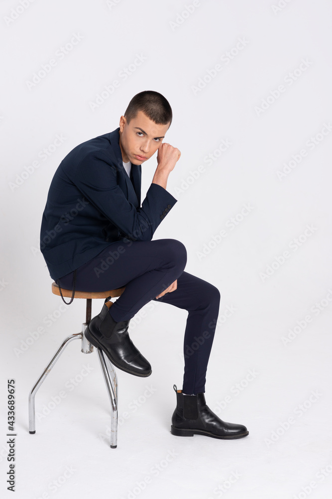 Serious male model in fashionable suit sitting on white background in ...