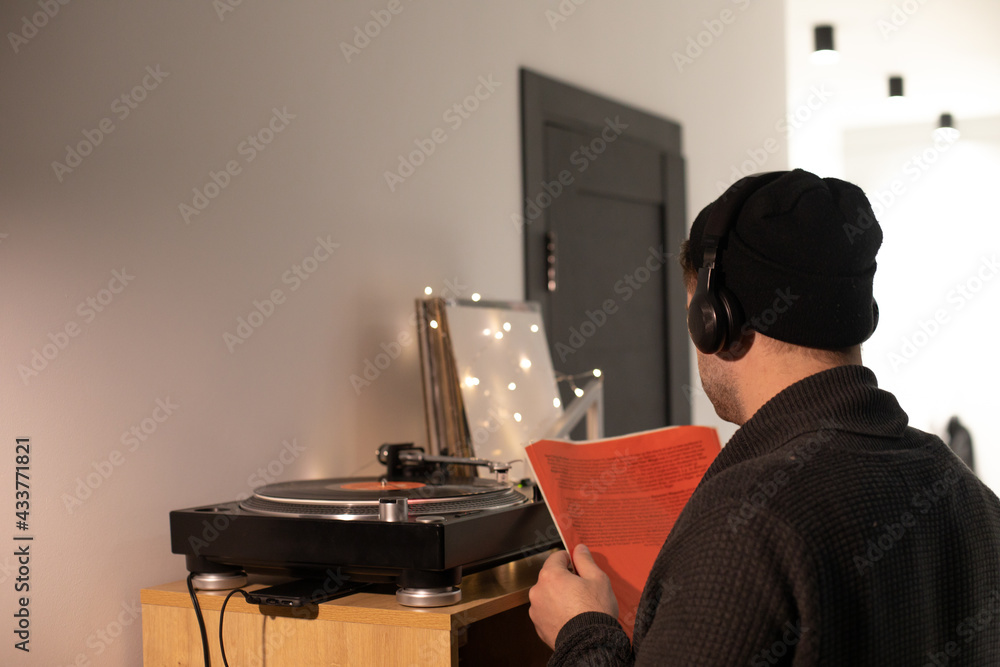 Young unshaven handsome hipster guy puts record on turntable from red ...