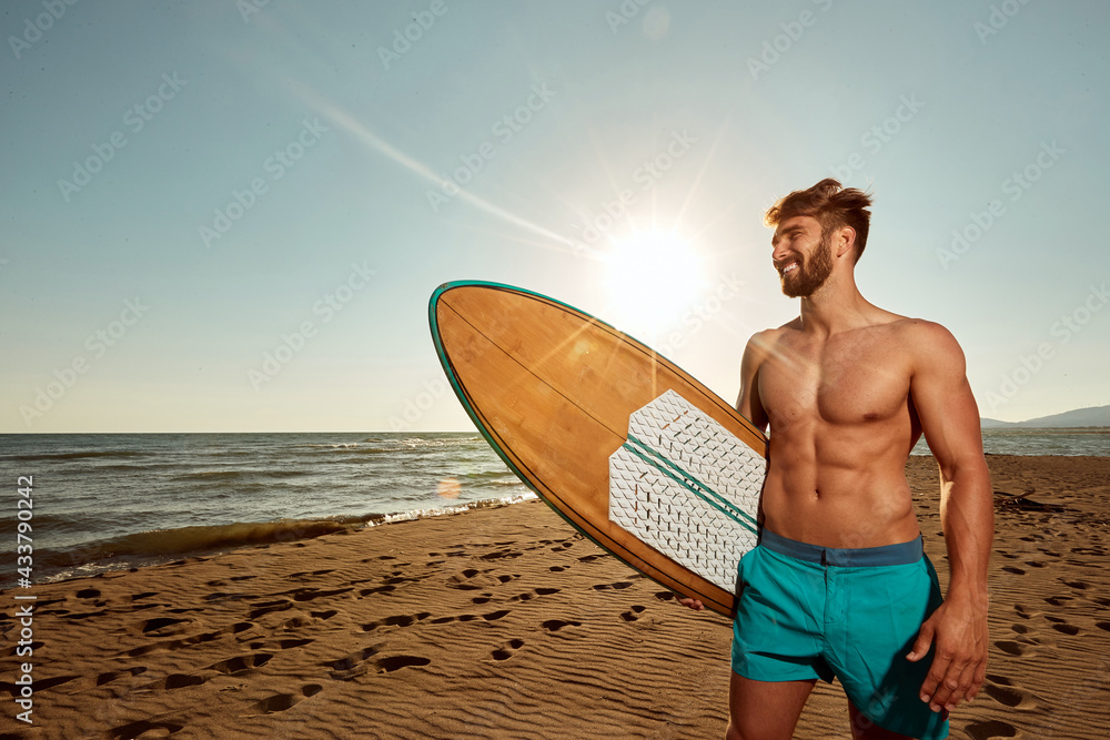 Young handsome male surfer holding a surfboard and watching a beautiful ...