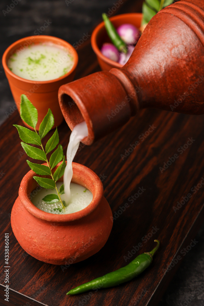 Pouring serving Spiced buttermilk in clay pot , chaas , chaach , moru ...