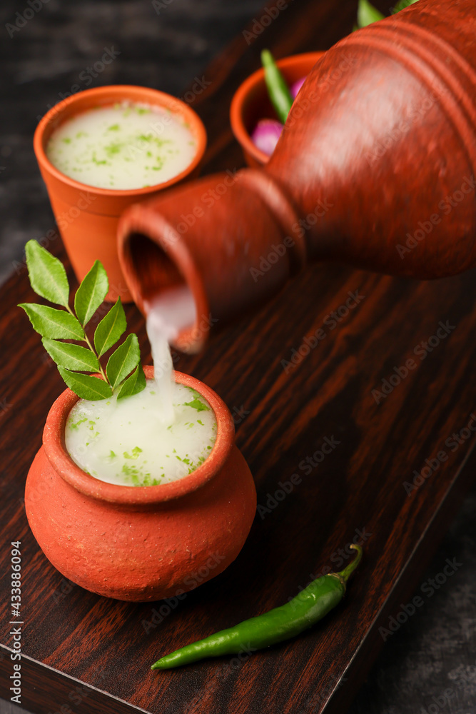 Pouring serving Spiced buttermilk in clay pot , chaas , chaach , moru ...