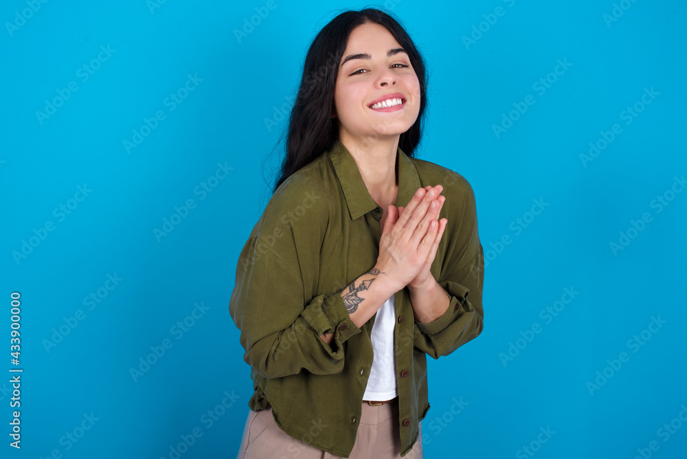 young beautiful tattooed girl standing against blue wall, feeling happy ...