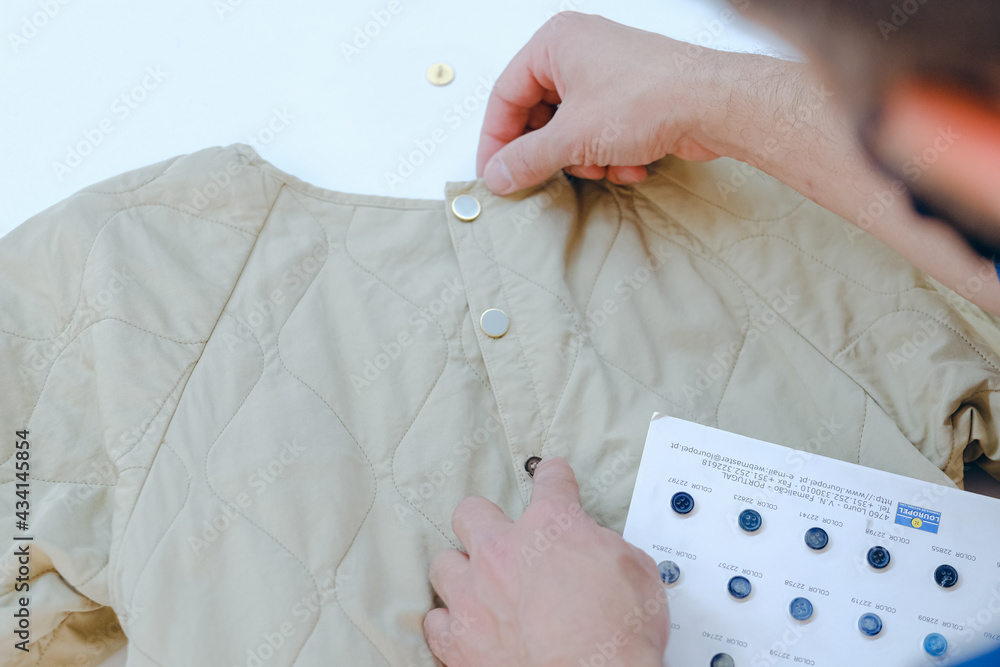 Female tailor hands putting buttons in brown fabric coat in a textile ...