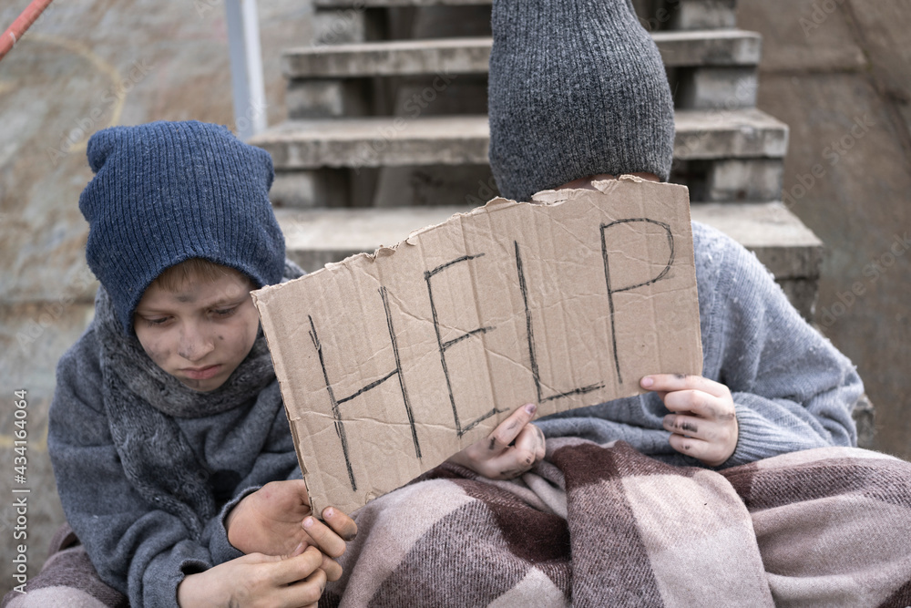 homeless boys sit with a help sign on the stairs in an abandoned place ...