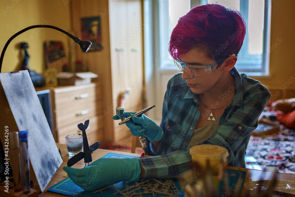 Geek teenage girl in protect eyeglasses engineering an airplane model ...