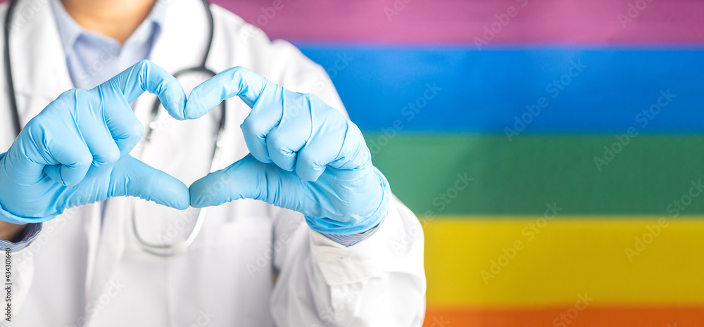 Doctor hand in blue gloves showing heart sign against the rainbow flag ...