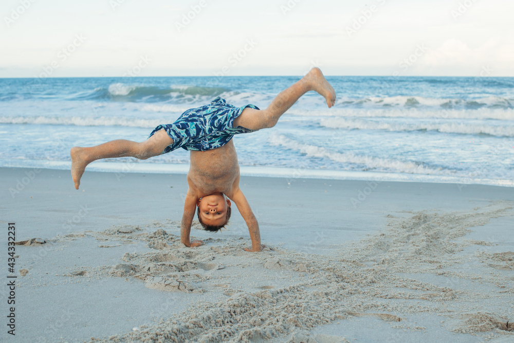 Boy doing a somersault on the sand on the beach. Exciting child having ...