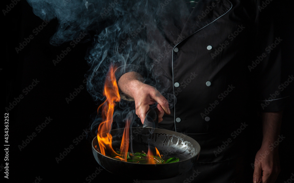 Chef cooking food in pan with fire flame on black background ...