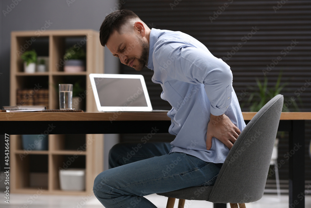 Man suffering from back pain while working with laptop in office ...