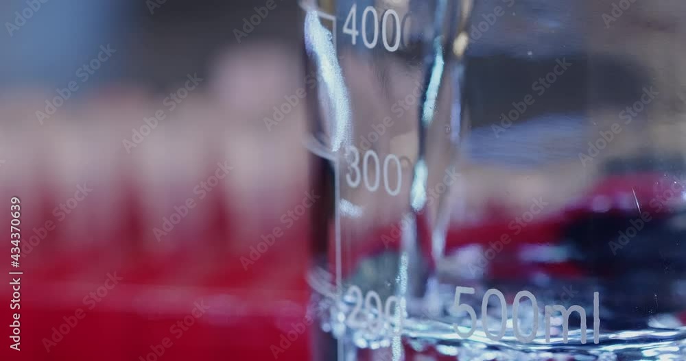 Pouring water into glass flask with measuring scale on blurred ...